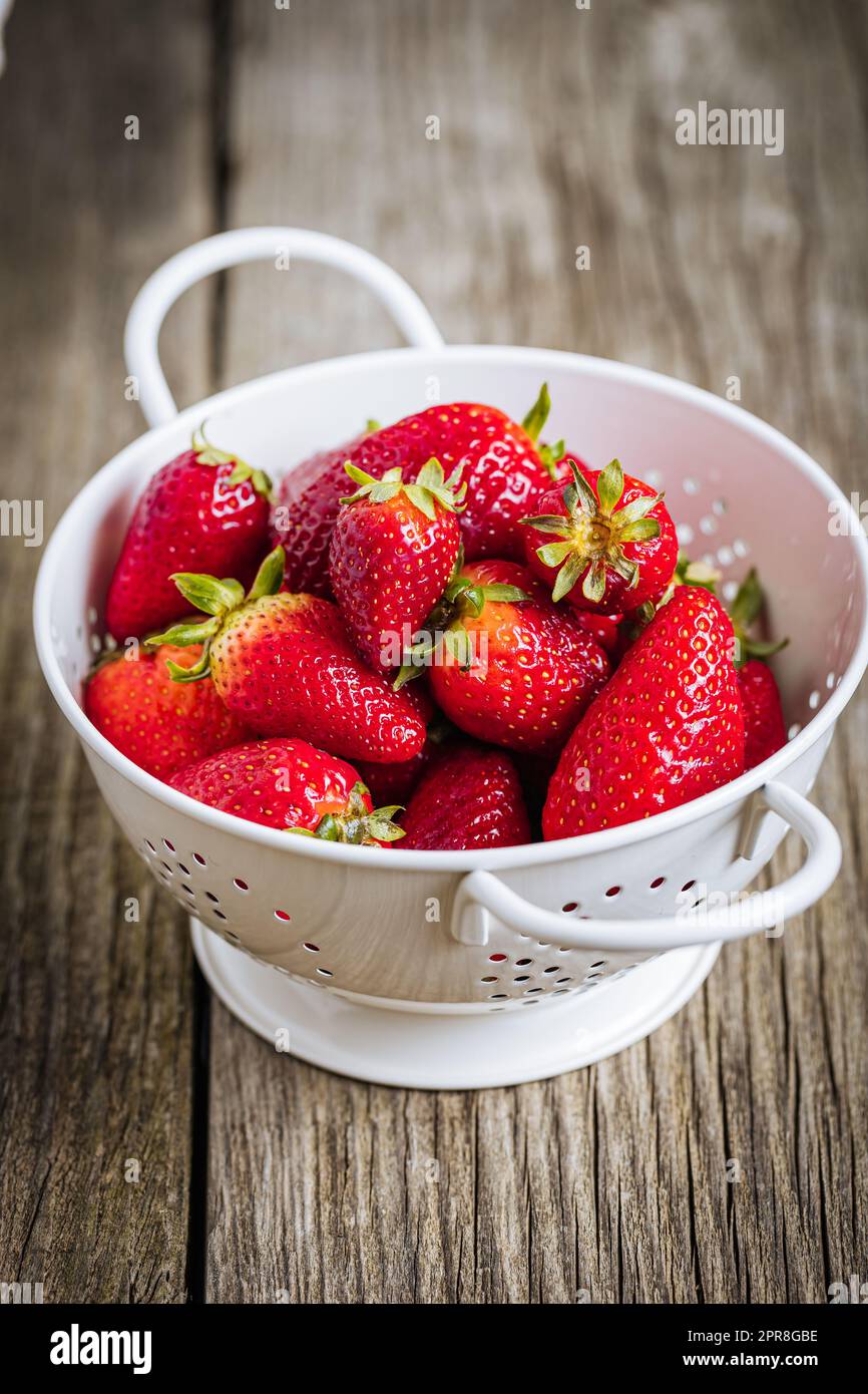 Strawberries in white colander placed on a rustic wooden background ...