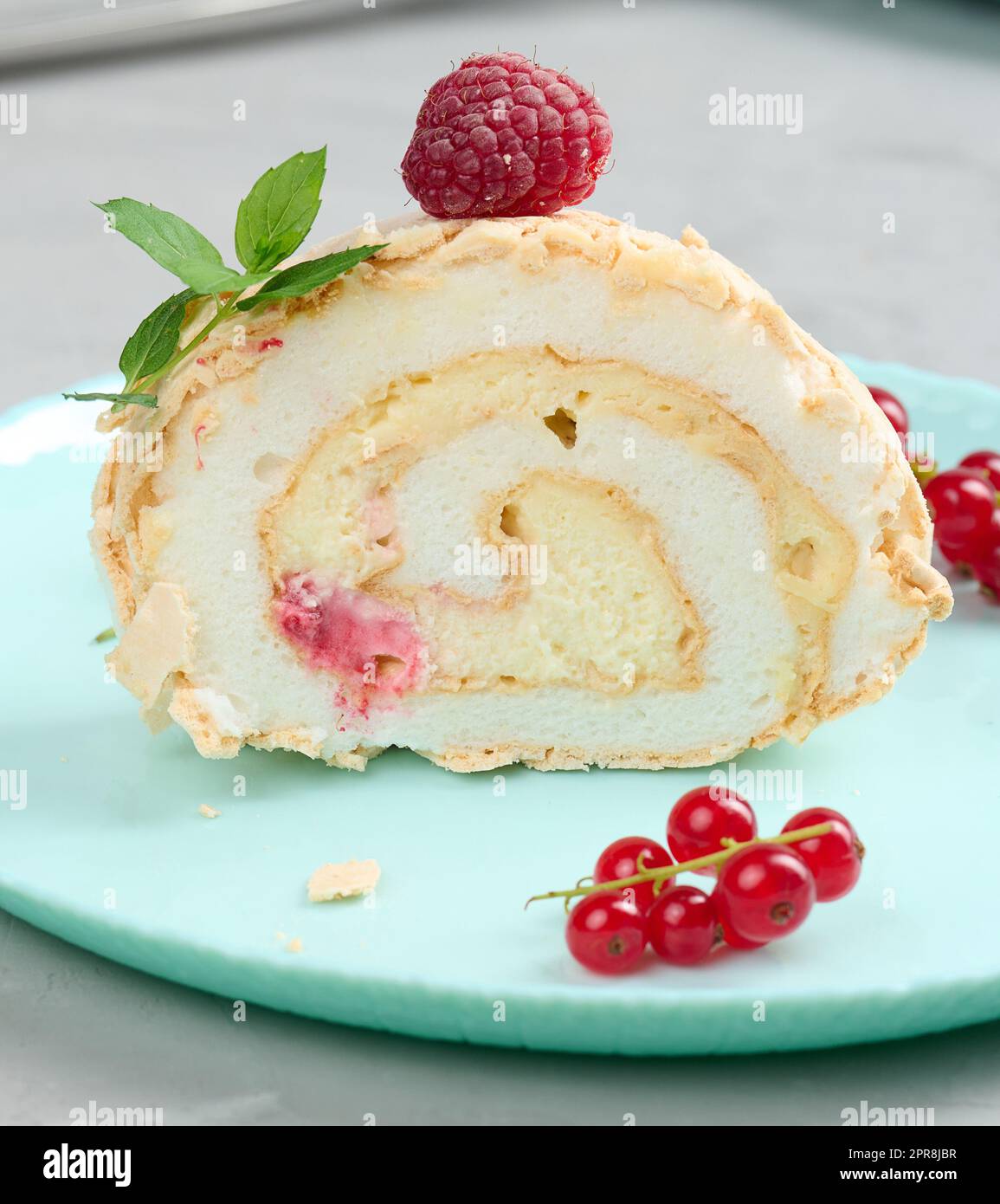 Baked meringue roll with red berries on a round plate, white background ...