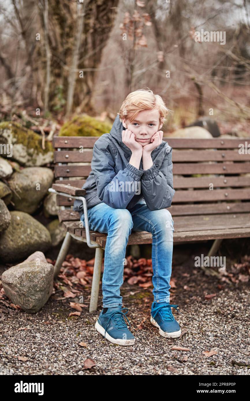 Bored teenage boy sitting alone outdoors on a park bench feeling sad ...