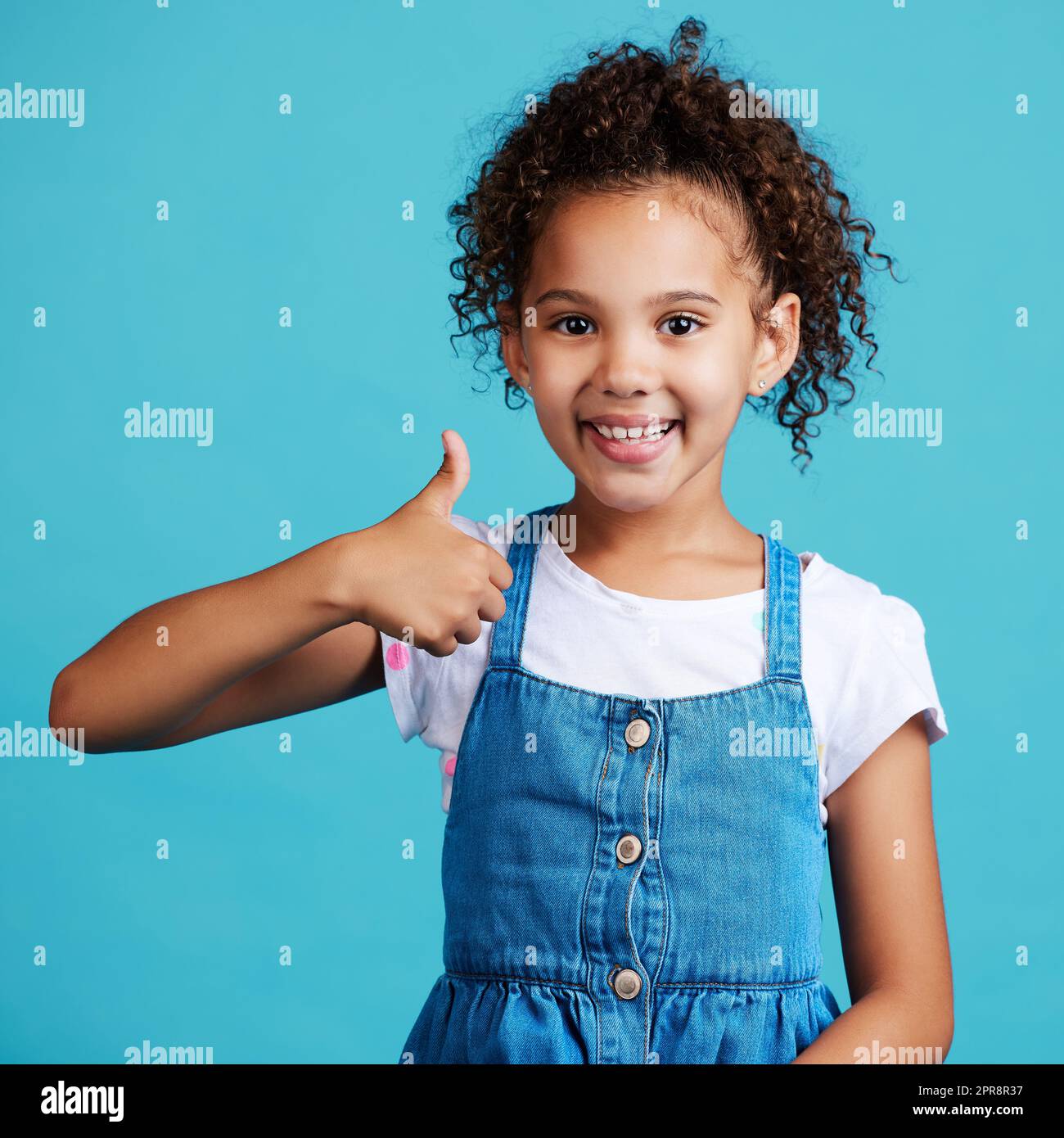 Im giving you the thumbs up. an adorable little girl showing thumbs up while standing against a ...