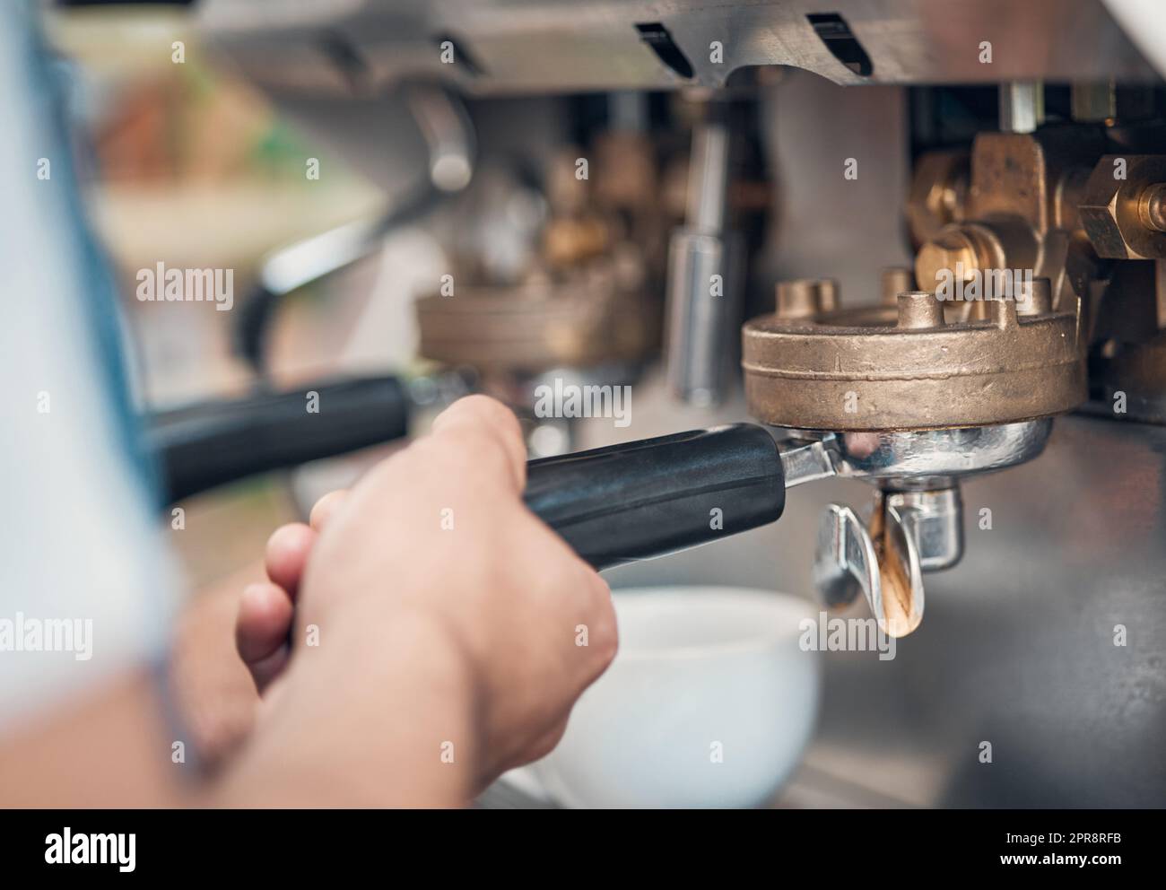 Closeup of a barista using a portafilter while preparing ground coffee to make a shot of ...