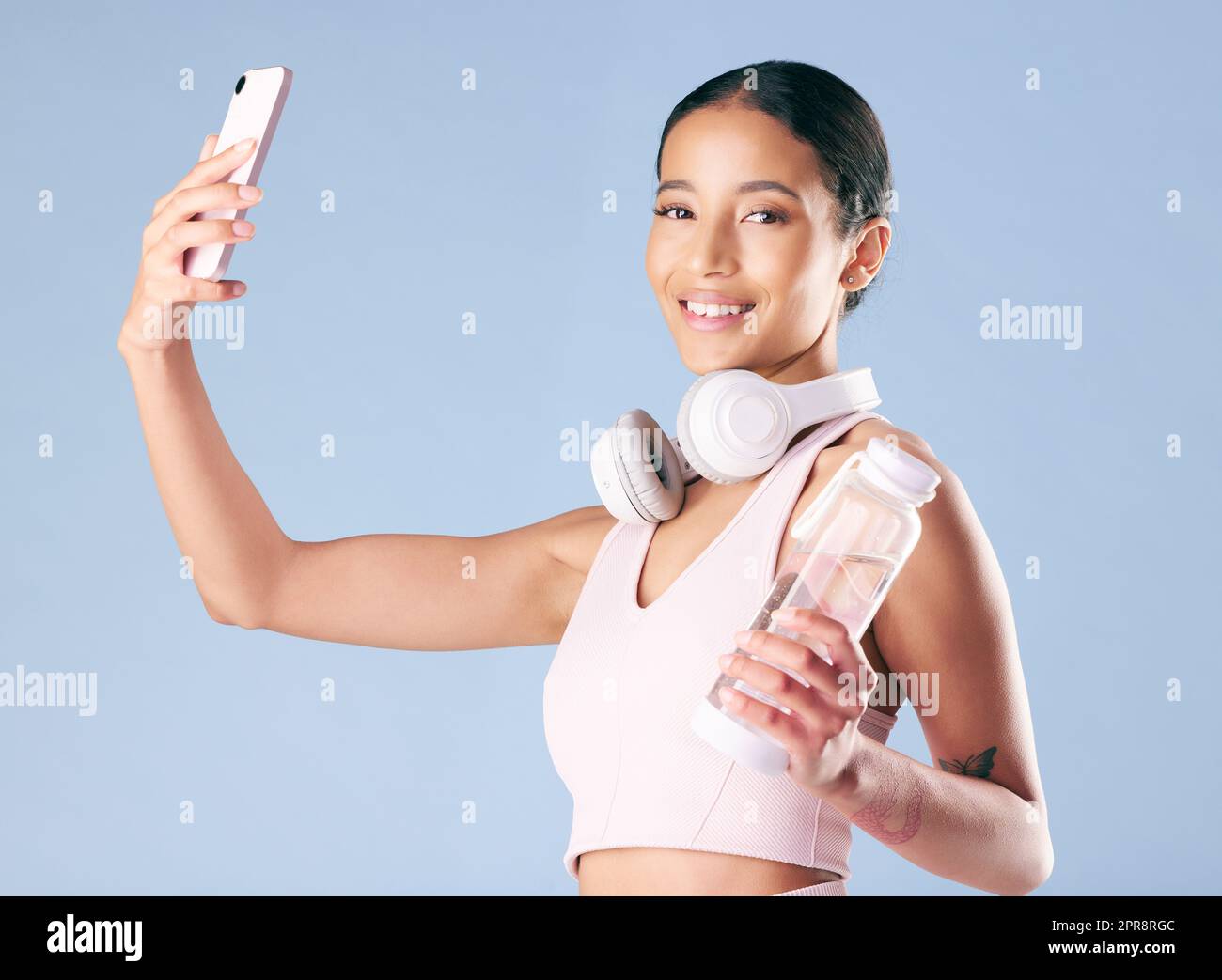 Mixed race fitness woman posing with her phone in studio against a blue ...