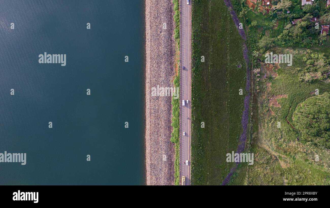 An aerial top view of a road near a lush park and blue water of Umiam ...
