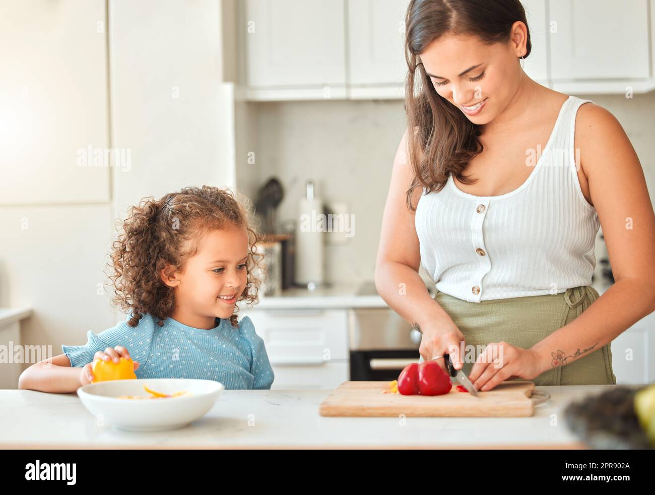 Adorable little girl watching her mother cook. Woman chopping vegetable ...