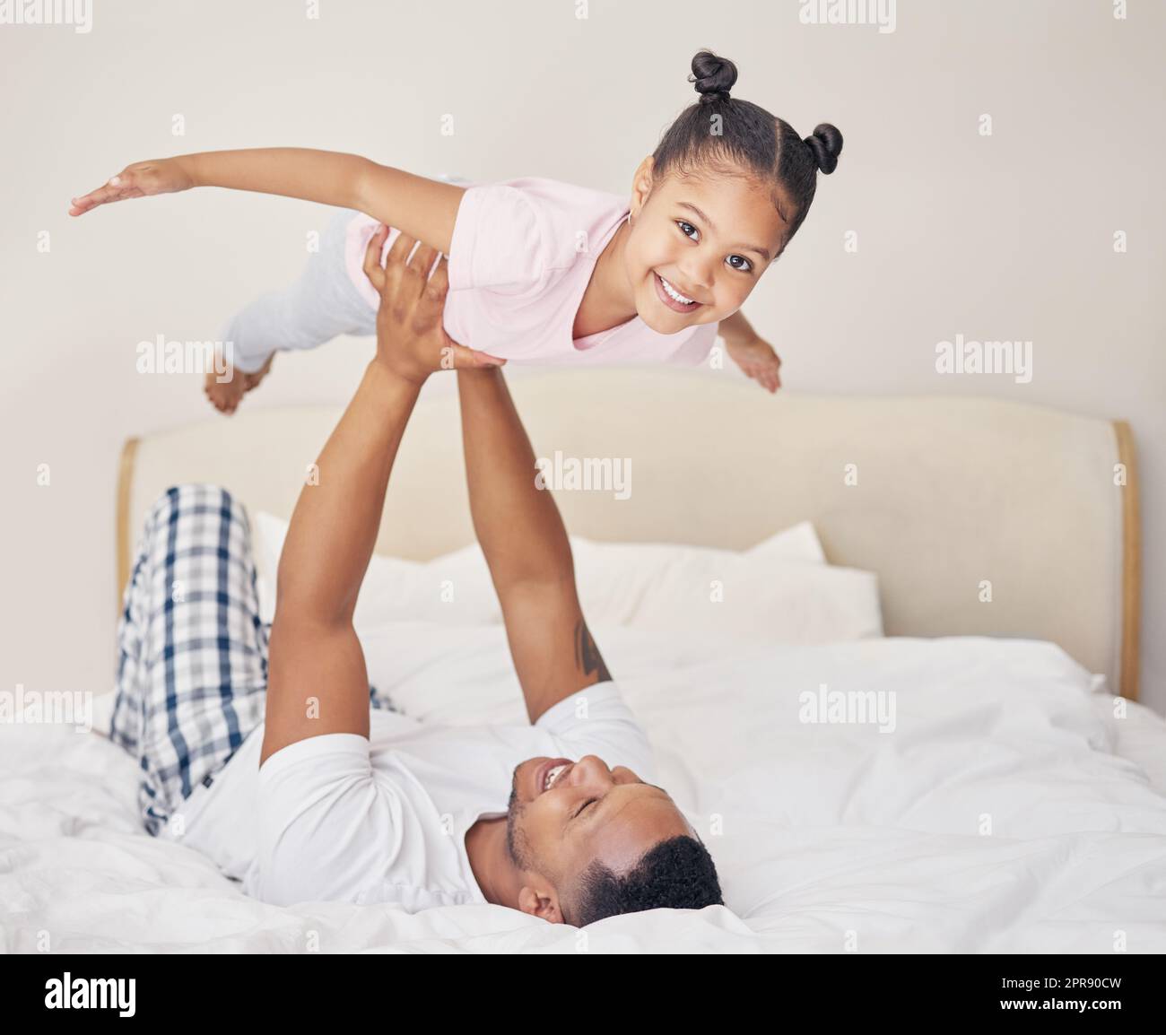 Joyful young father lying on bed, lifting excited happy little child ...