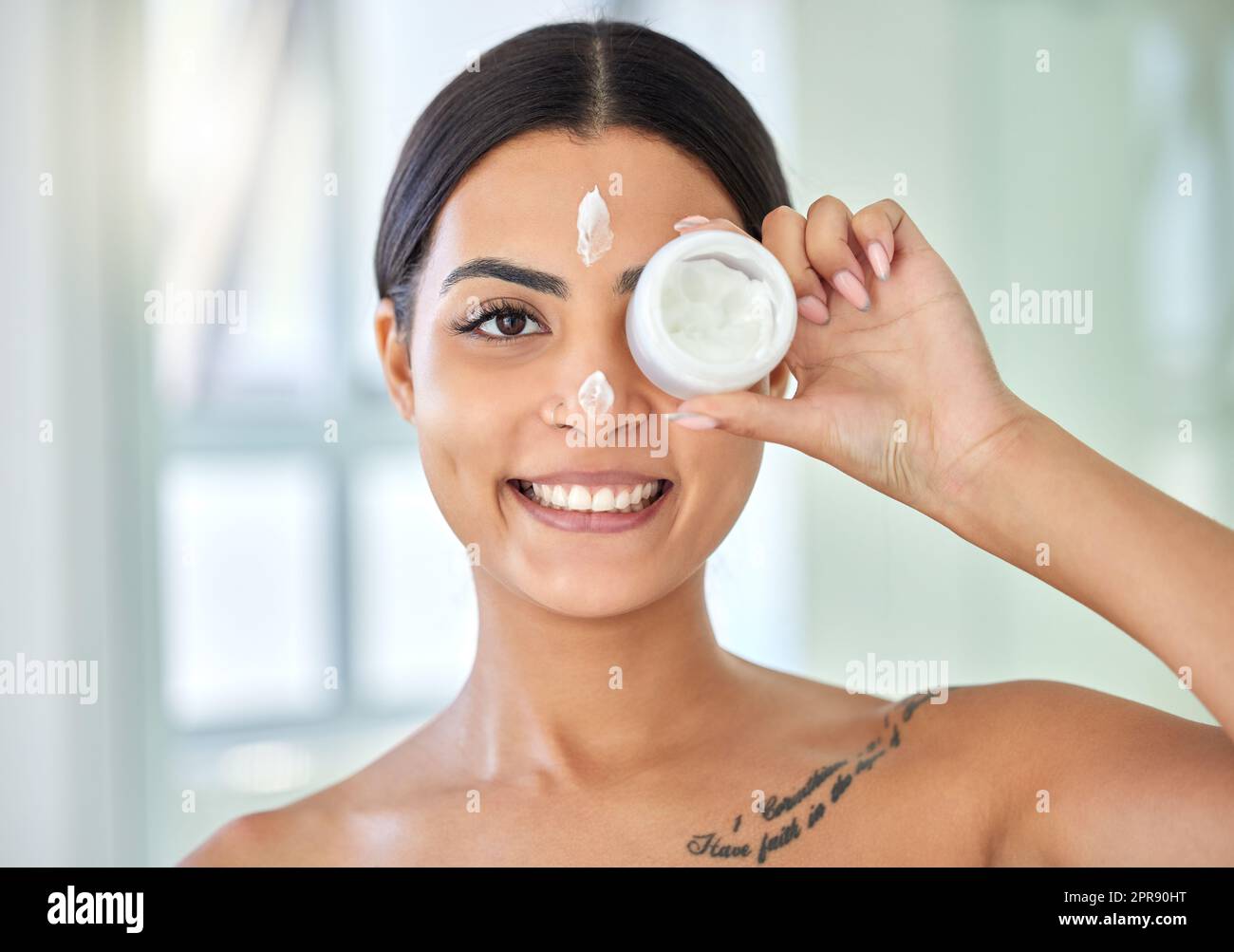 Eye just love moisturising my face. a young woman applying cream to her face in a bathroom at ...