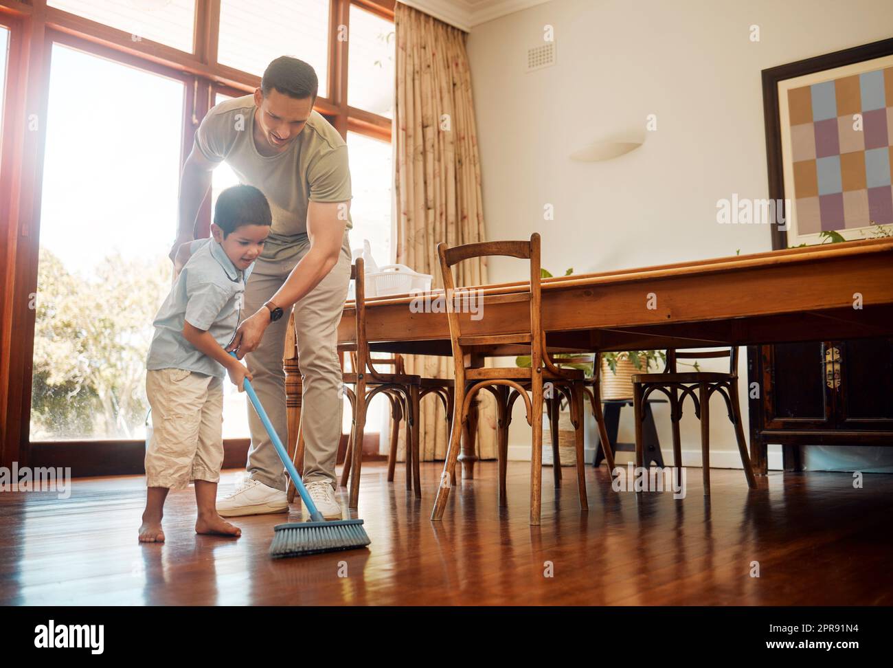 Mixed race father helping little boy sweep dust and dirt on wooden ...