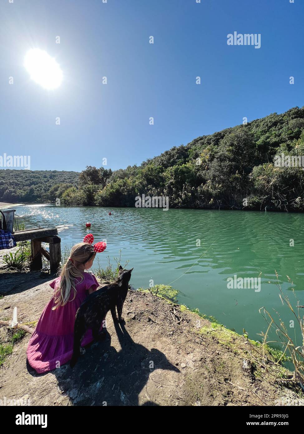 Little girl with Minnie Mouse ears on her head sits on the river bank ...