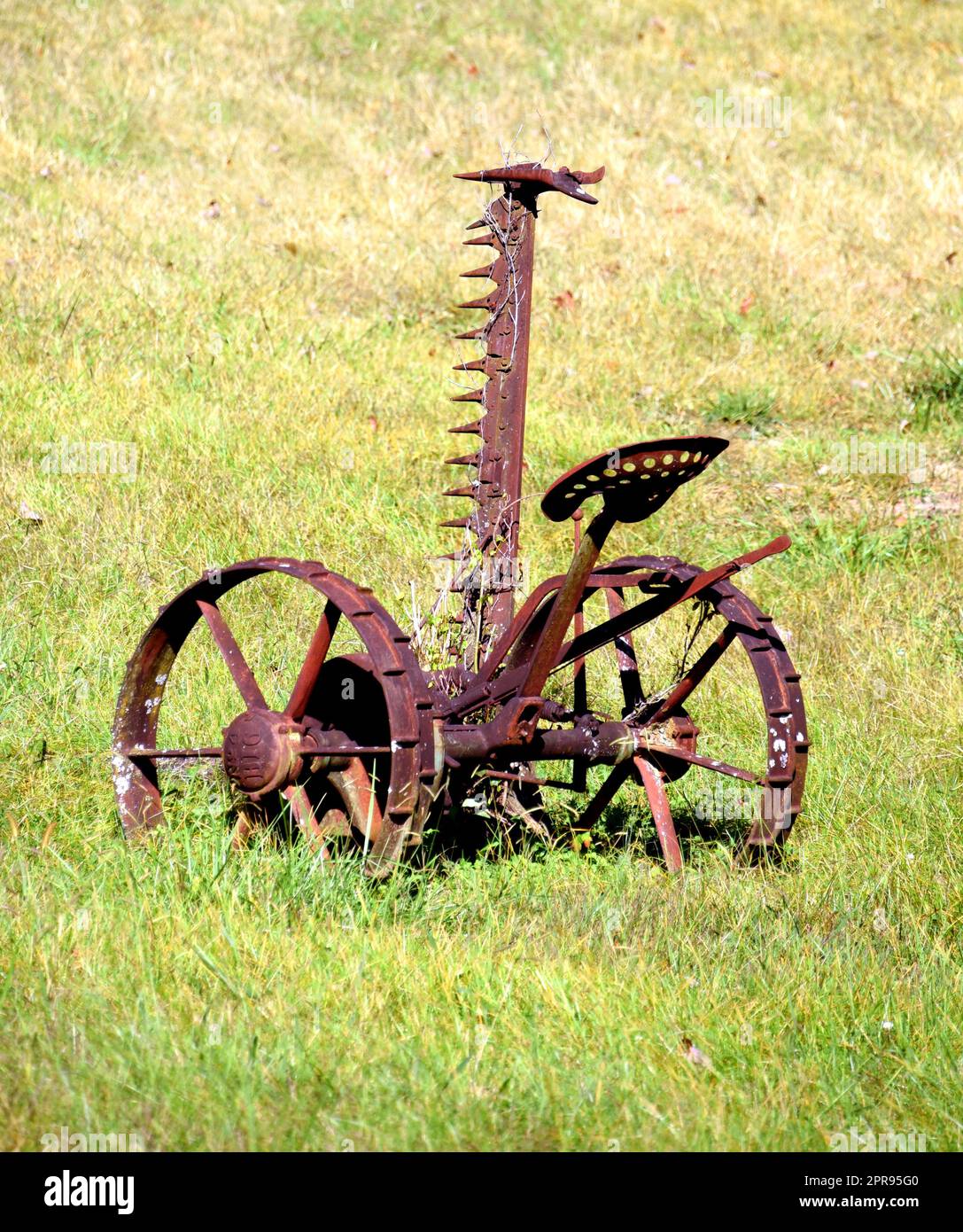 Old mower. with seat, sits rusting in field. Mower blade stands upright ...