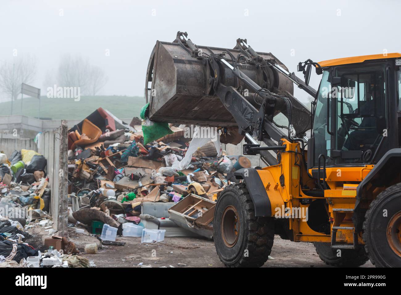 Yellow wheel loader, with lifted scrap grapple, moving along the ...