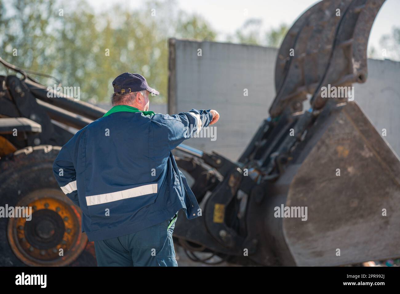 Male worker pointing on wheel loader and the garbage heap at a landfill ...