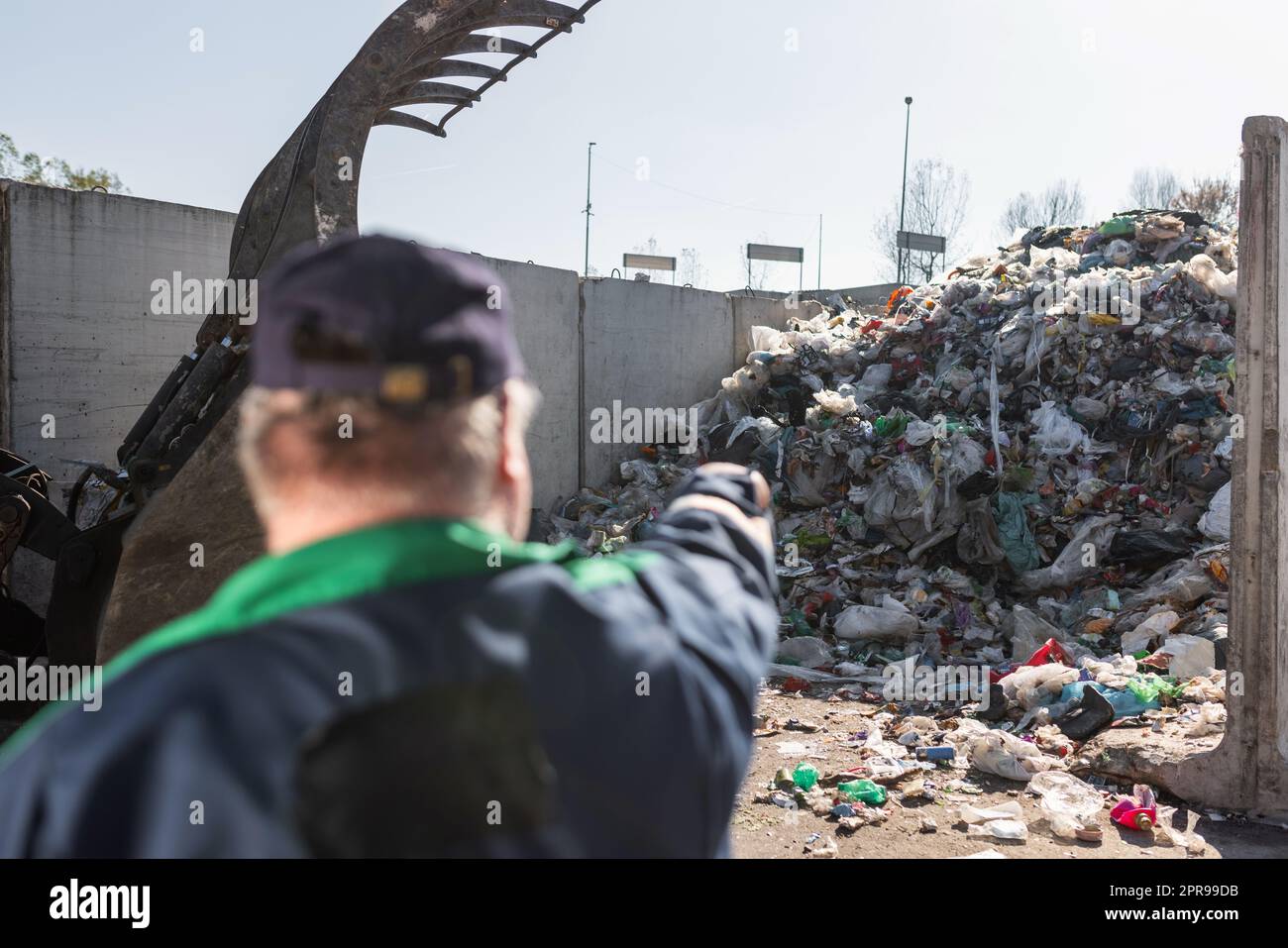 Landfill worker directing skid steer loader on the garbage heap. Waste ...
