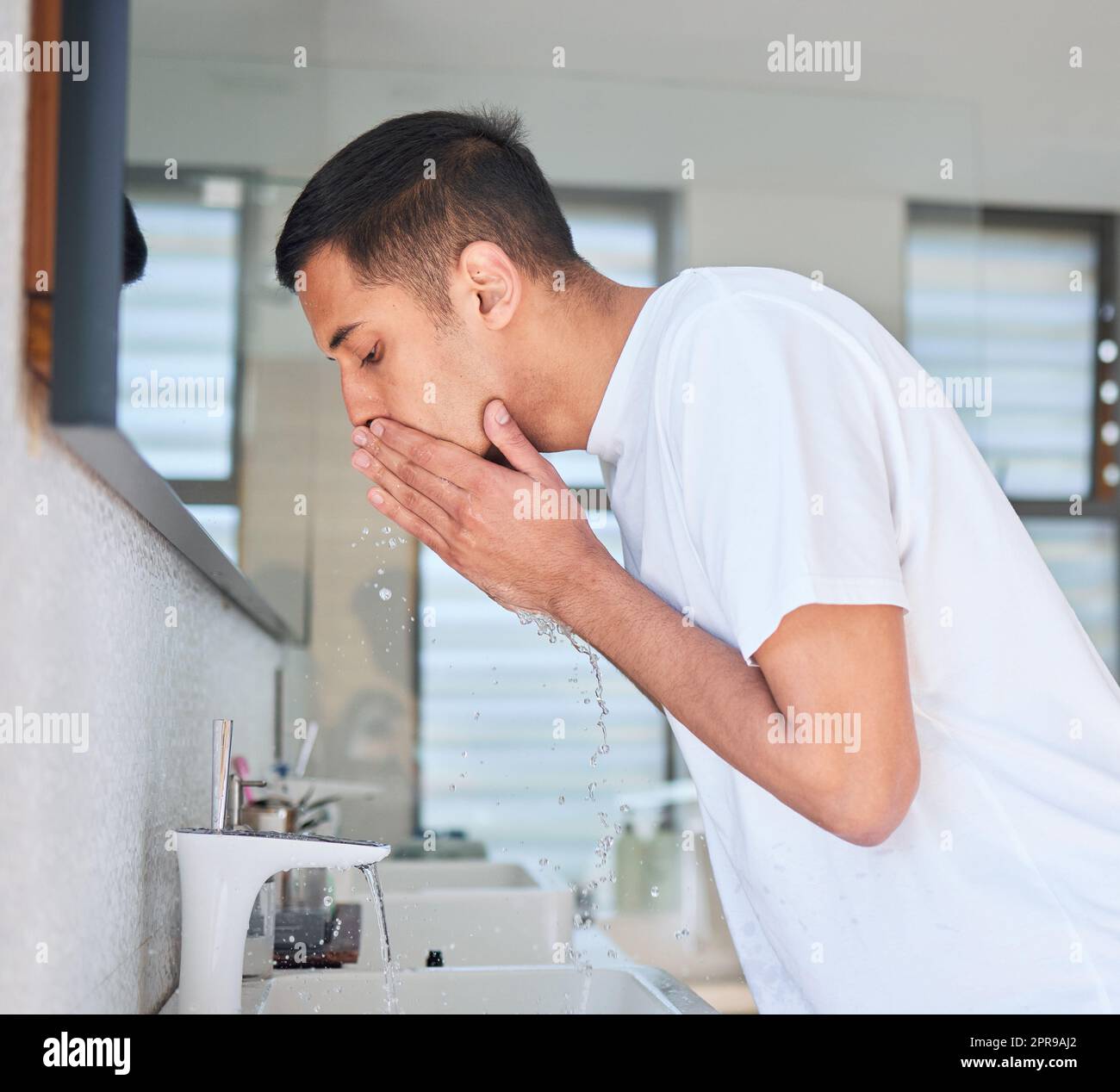 Nothing feels better than having a clean face. a young man washing his face in a bathroom at ...