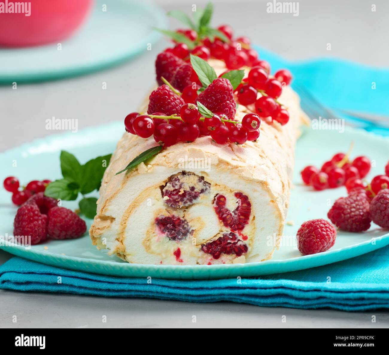 Baked meringue roll with red berries on a round plate, white background ...