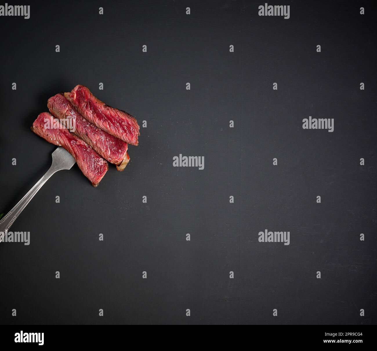 Fried pieces of beef strung on an iron large fork, black background ...