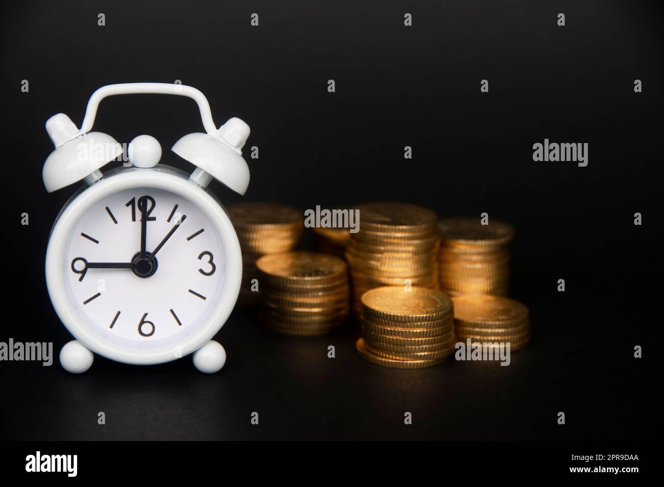 White alarm clock with gold coins isolated on dark background. Copy ...