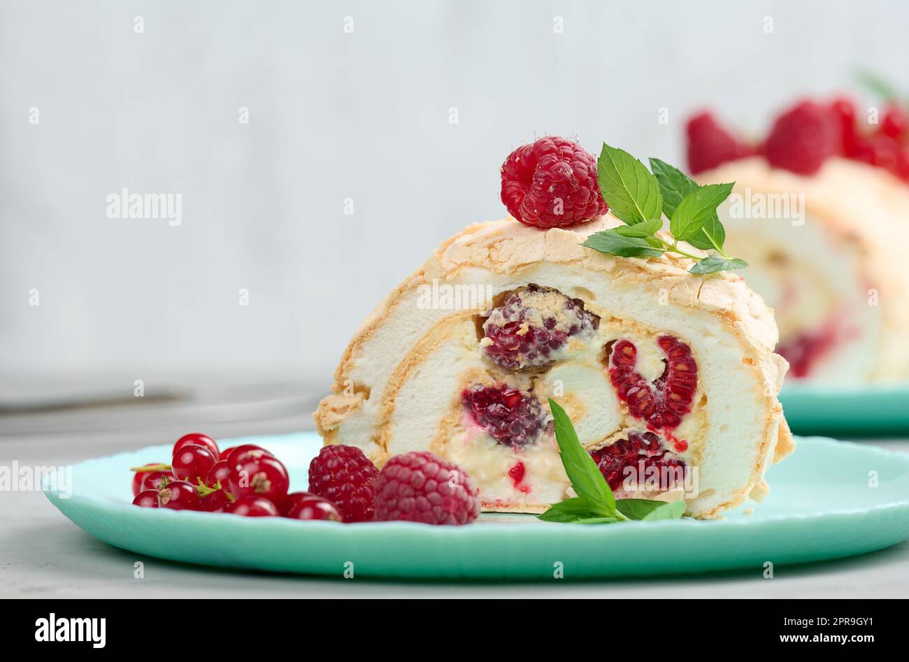 Baked meringue roll with red berries on a round plate, white background ...