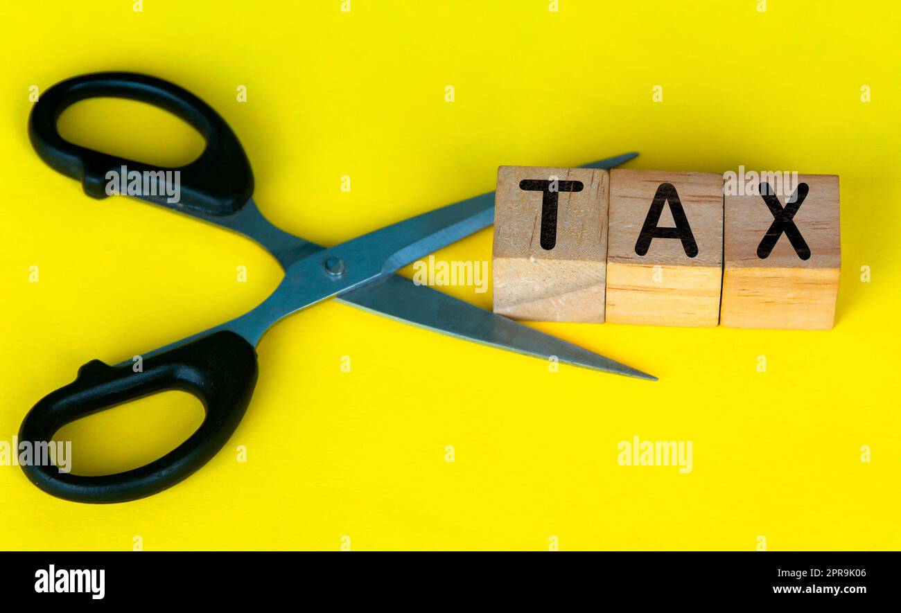Scissor cutting wooden blocks with text TAX. Cutting tax expenses ...