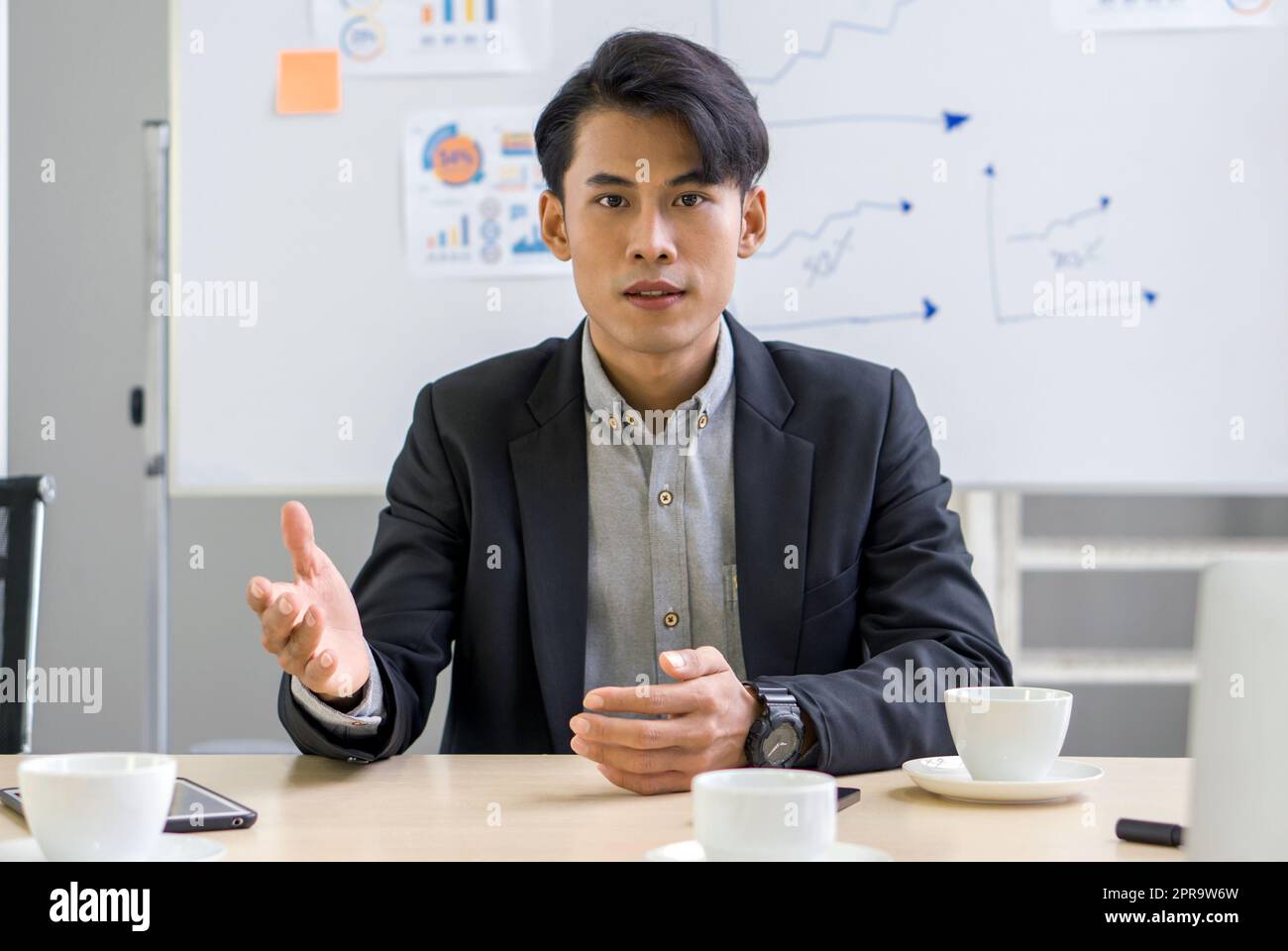 Asian businessman in black suit looking at camera, recording self ...