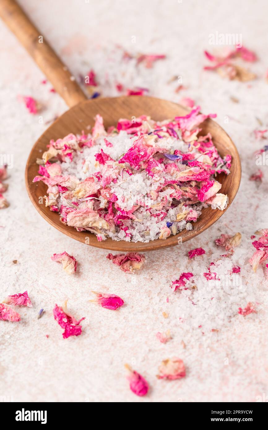 See salt wih with dried flower petals in wooden scoop on pink marble ...
