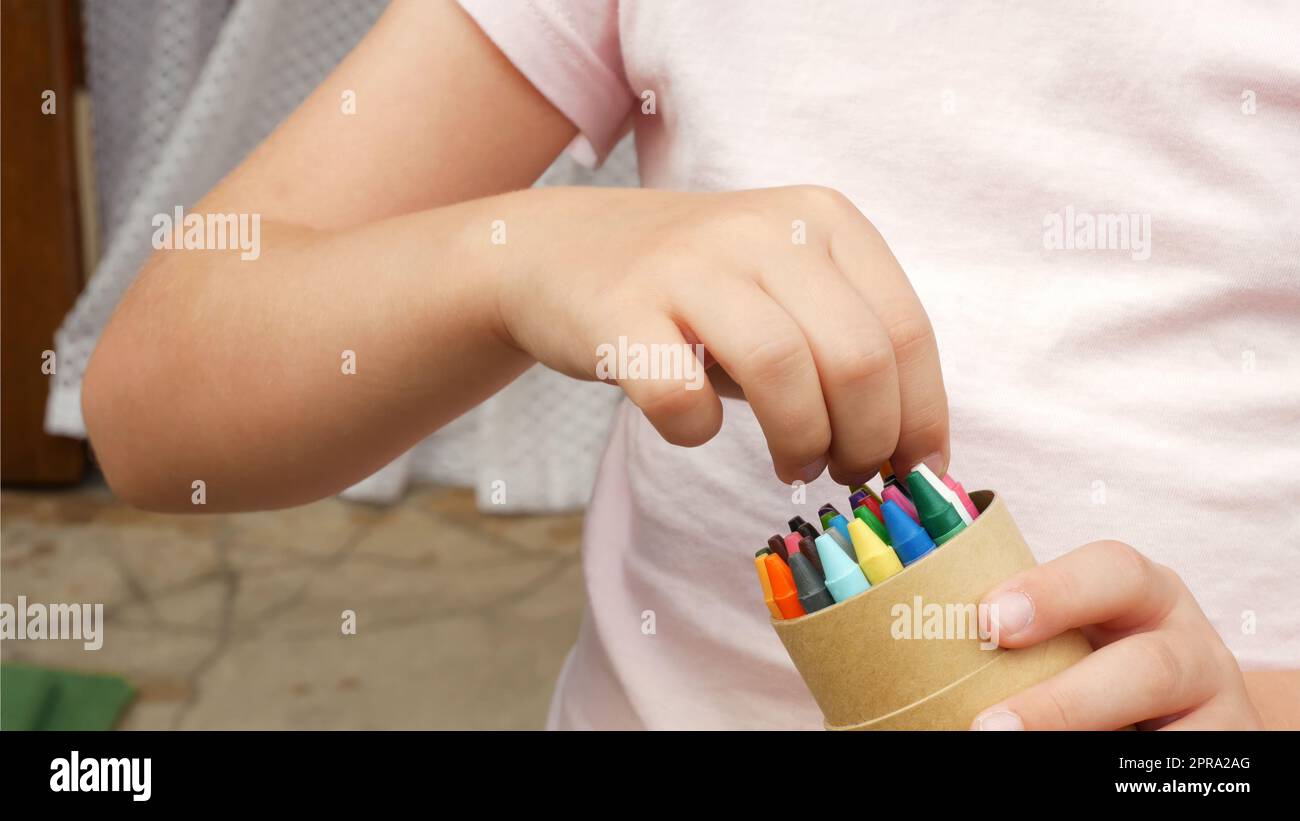 Anonymous child, school age girl holding a box of crayons choosing one ...