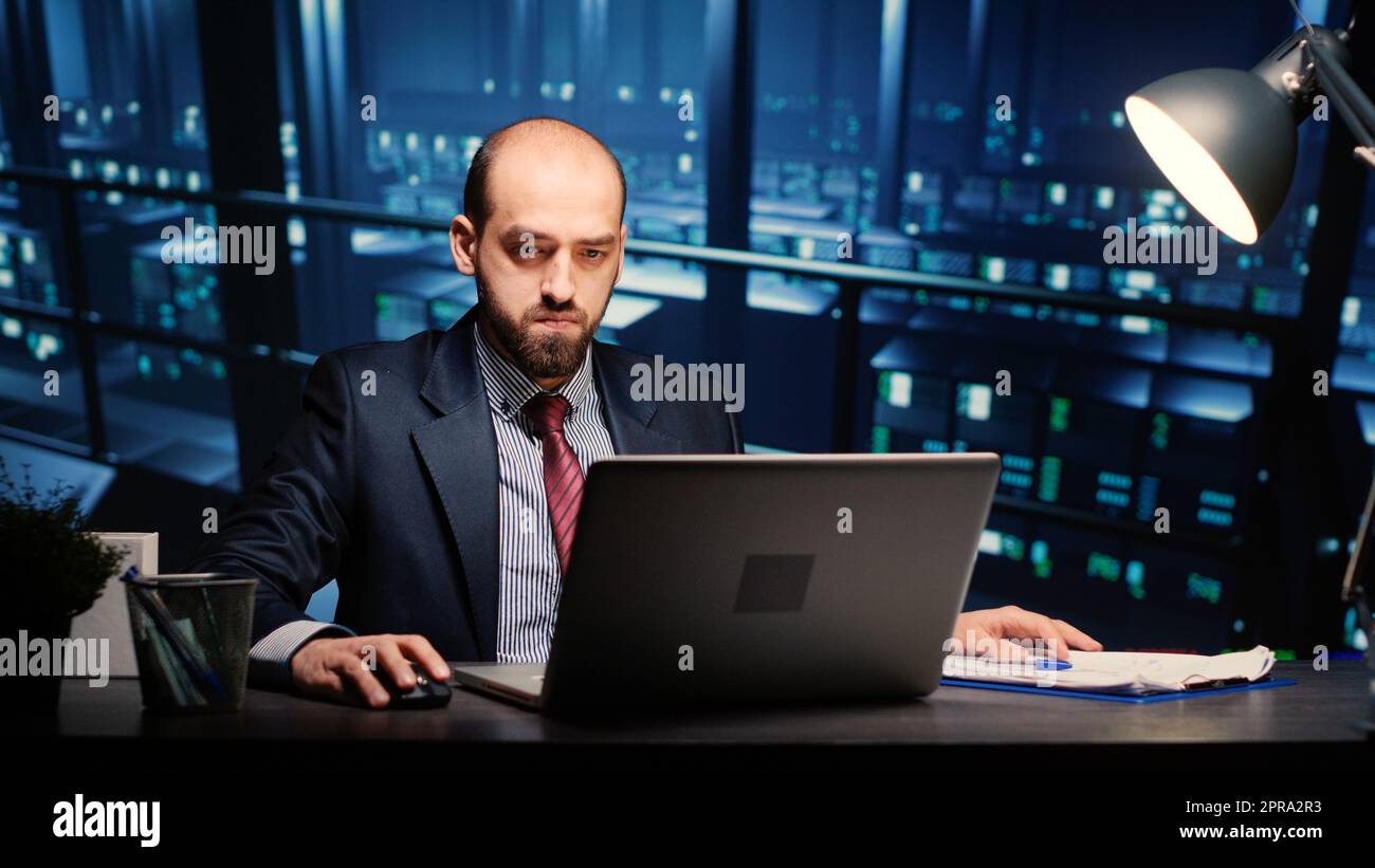 Male infrastructure engineer working in render farm running diagnostics on mainframe computer ...