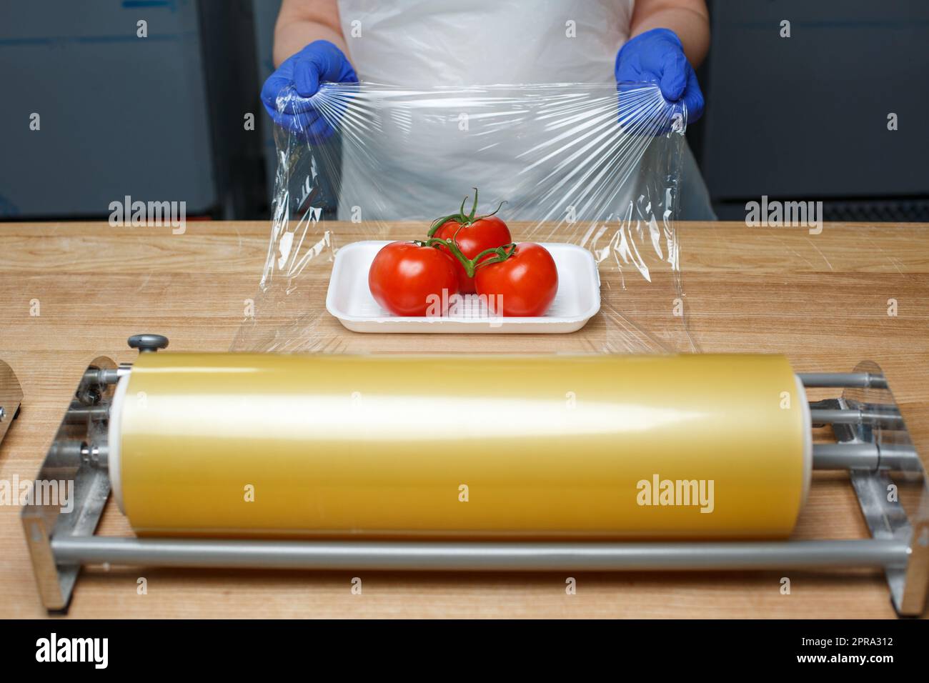 Unknown worker wraps in food transparent film tomatoes lying on white ...