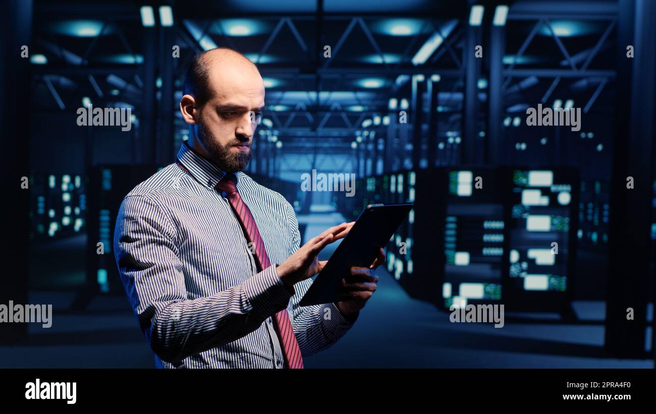 Information security officer working in data center with tablet, analyzing server rack cabinets ...