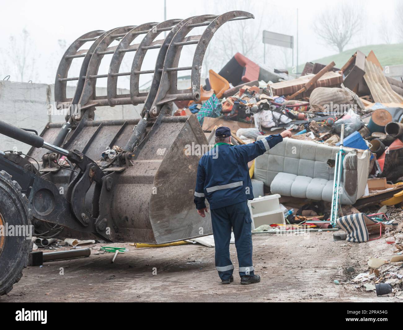 Landfill worker directing skid steer loader on the garbage heap, rear ...