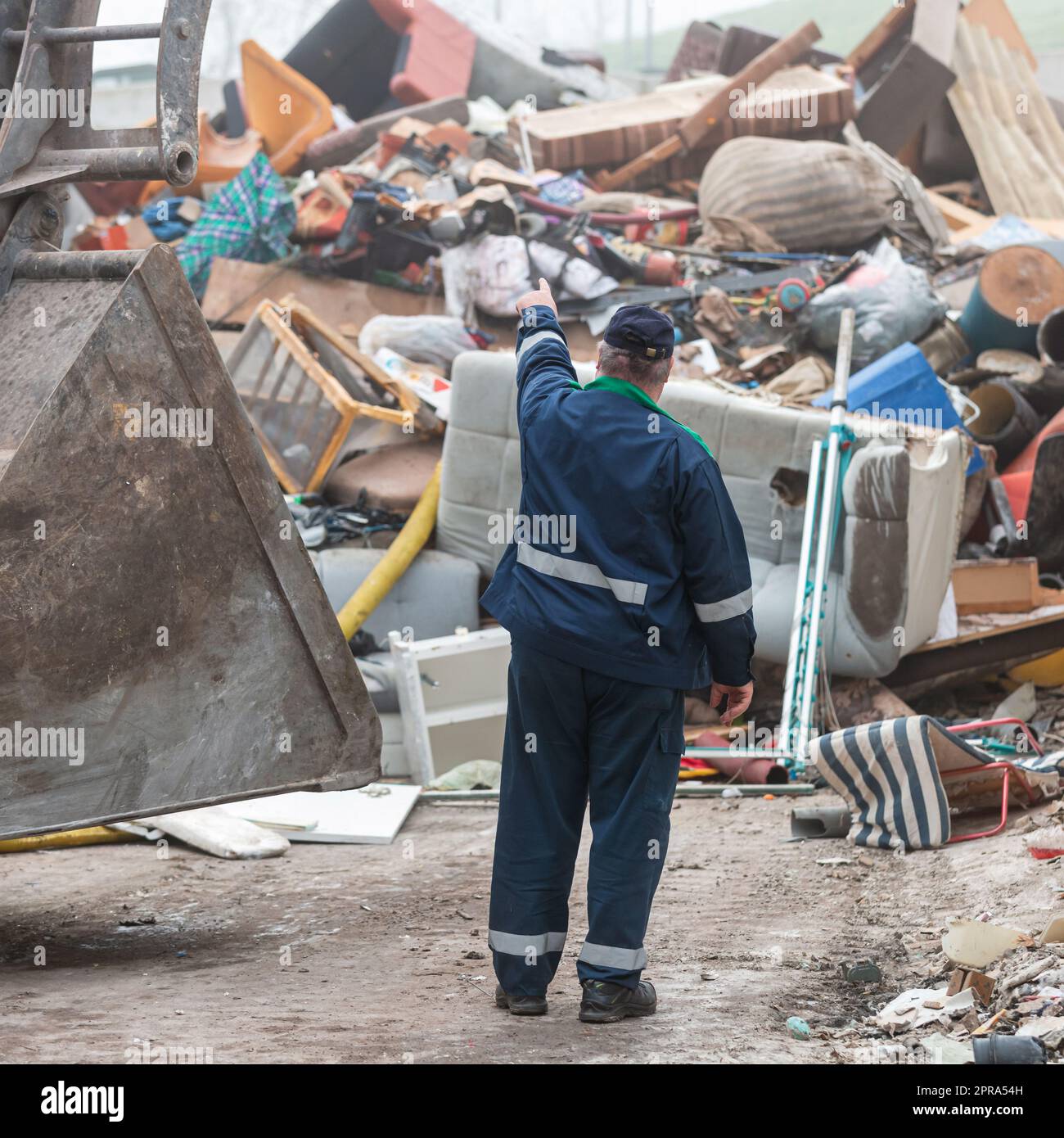 Worker at a recycling center standing near a bucket loader, looking and ...