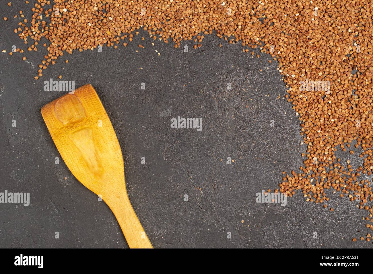 top view brown raw buckwheat with wooden spoon on the dark background ...