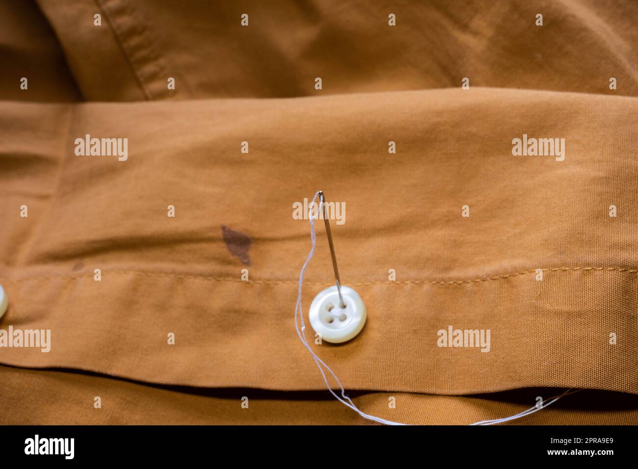 sewing on a button with a sewing needle and thread Stock Photo - Alamy