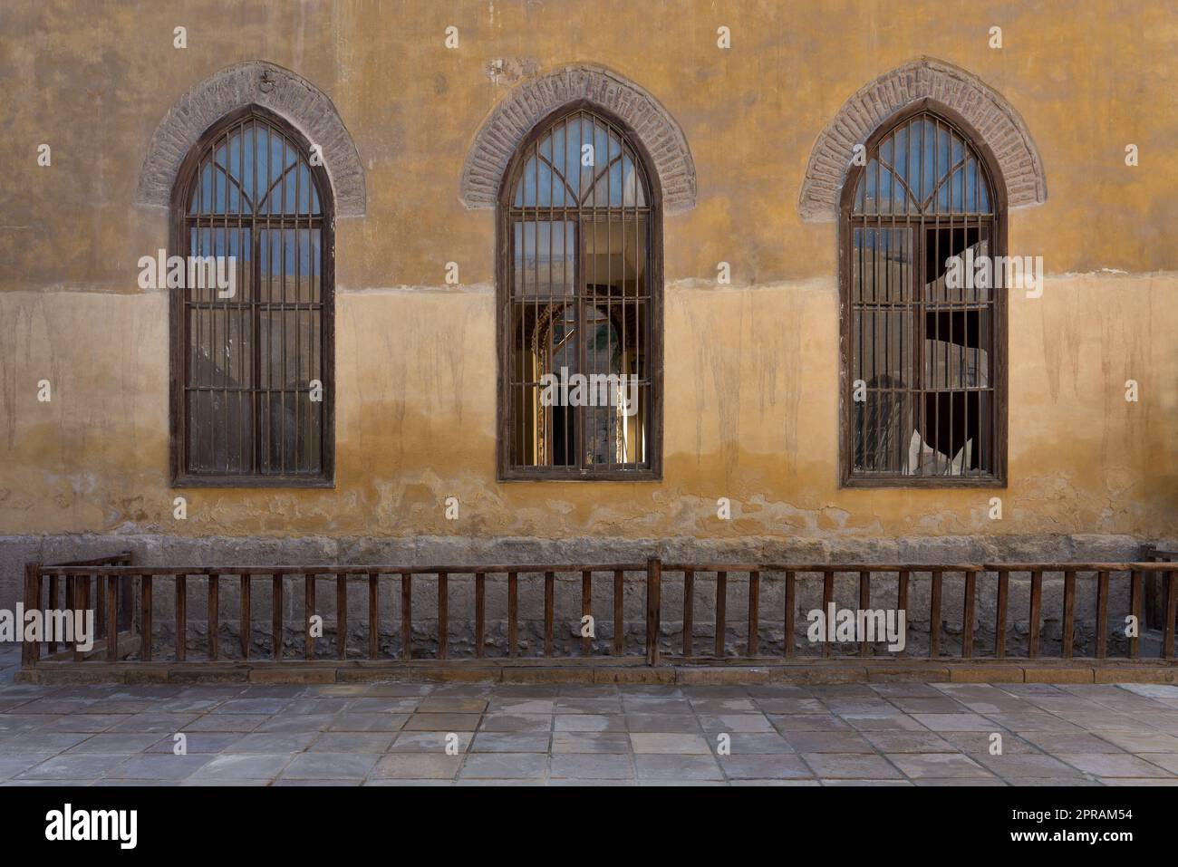 Wooden arched window with wrought iron grid over yellow stone bricks ...