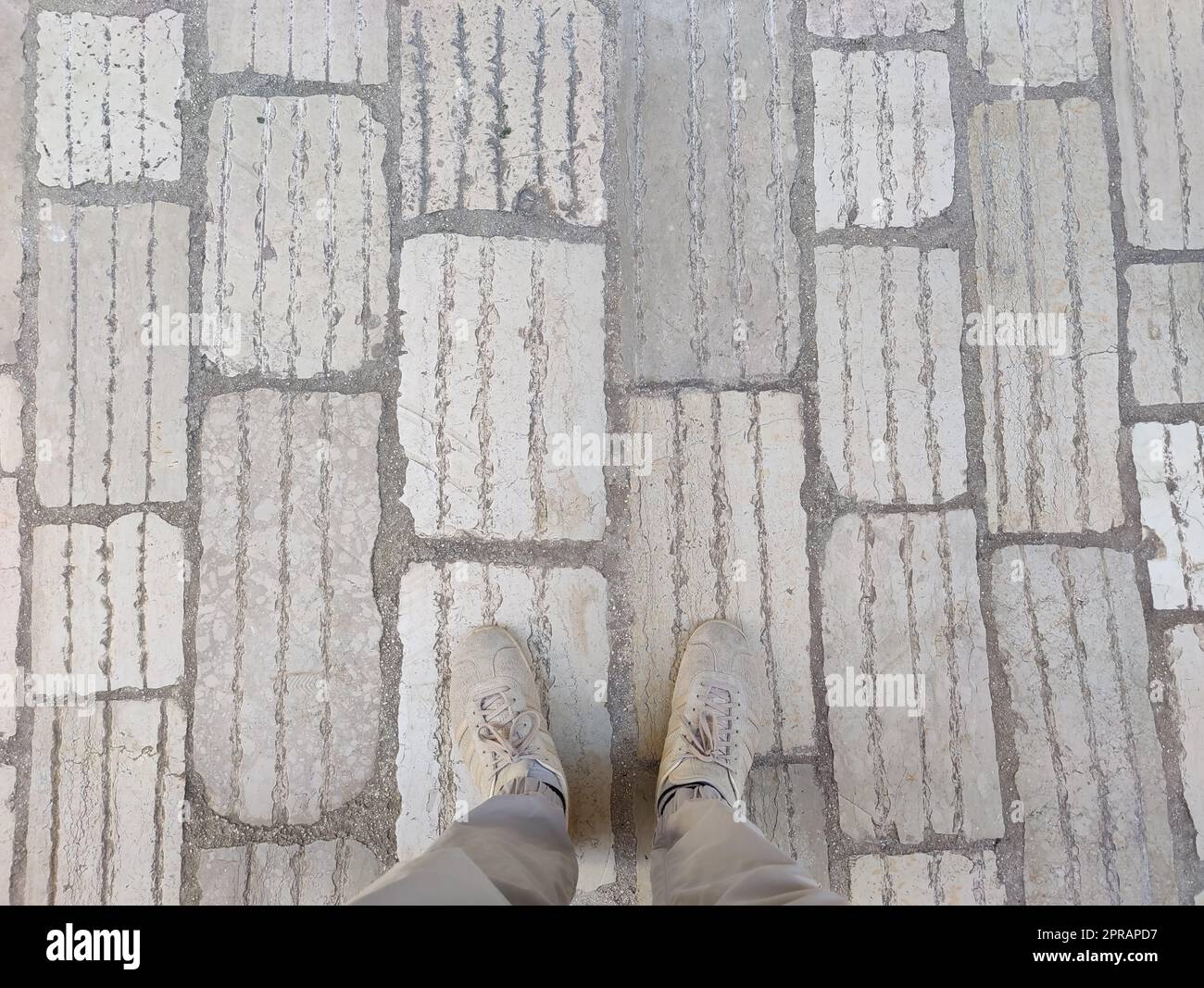 Top down view of male legs in grey trousers and beige sneakers on ...