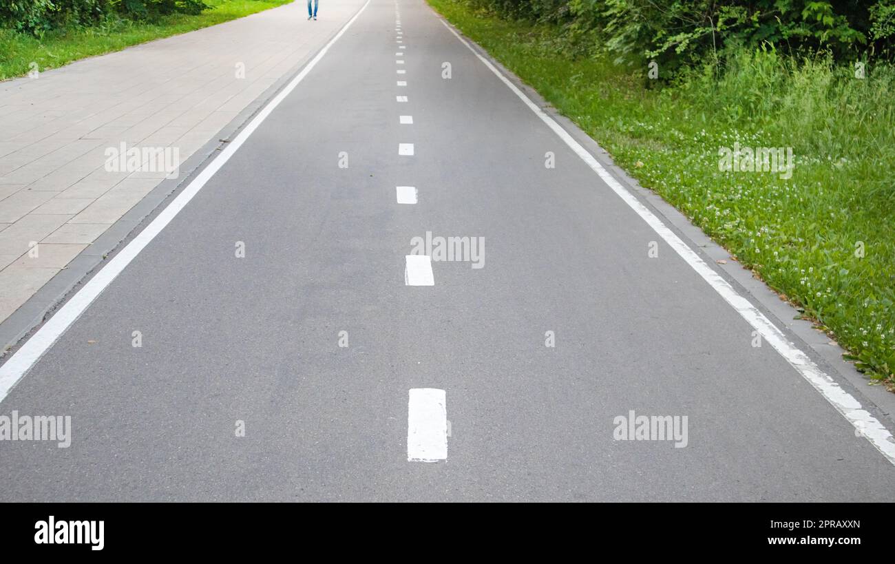 Close-up of an asphalt road with an intermittent marking line and grass ...