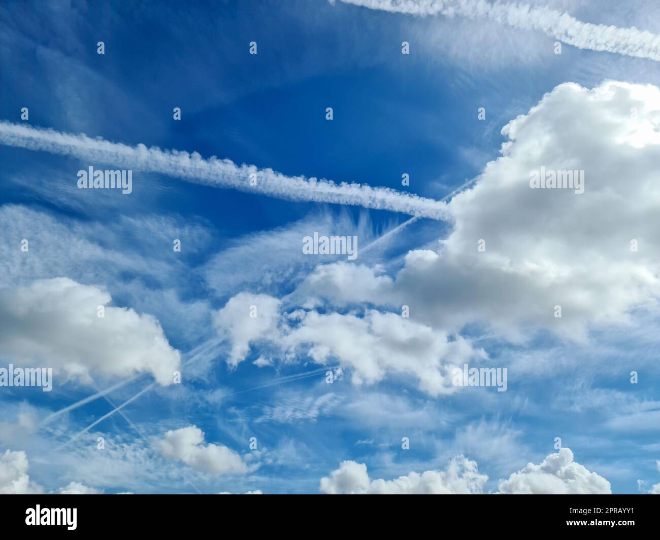 Aircraft condensation contrails in the blue sky inbetween some clouds ...