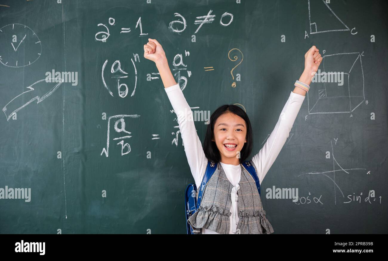 Asian school girl in uniform on classroom raised arms to successful ...