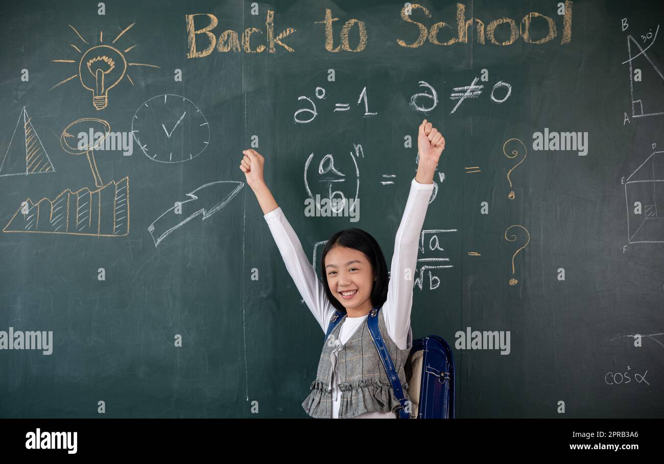 Asian school girl in uniform on classroom raised arms to successful ...