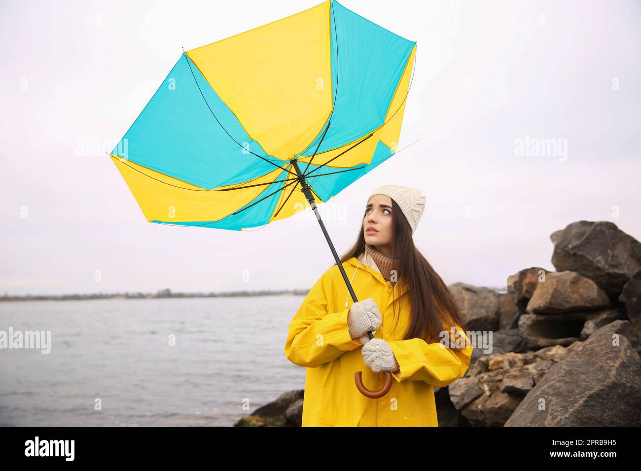 Woman in yellow raincoat with umbrella caught in gust of wind near ...