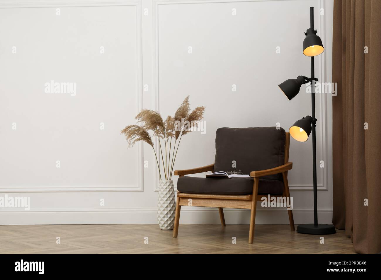 Stylish armchair with book, floor lamp and spikes near white wall ...