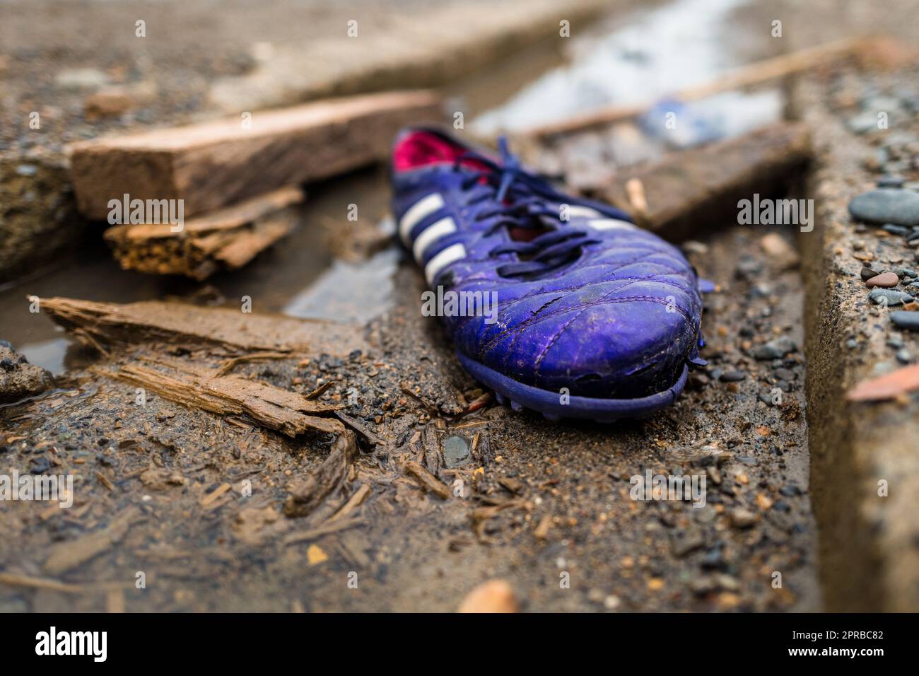 A worn out and leaky football cleat is seen lying beside a dirt playing ...