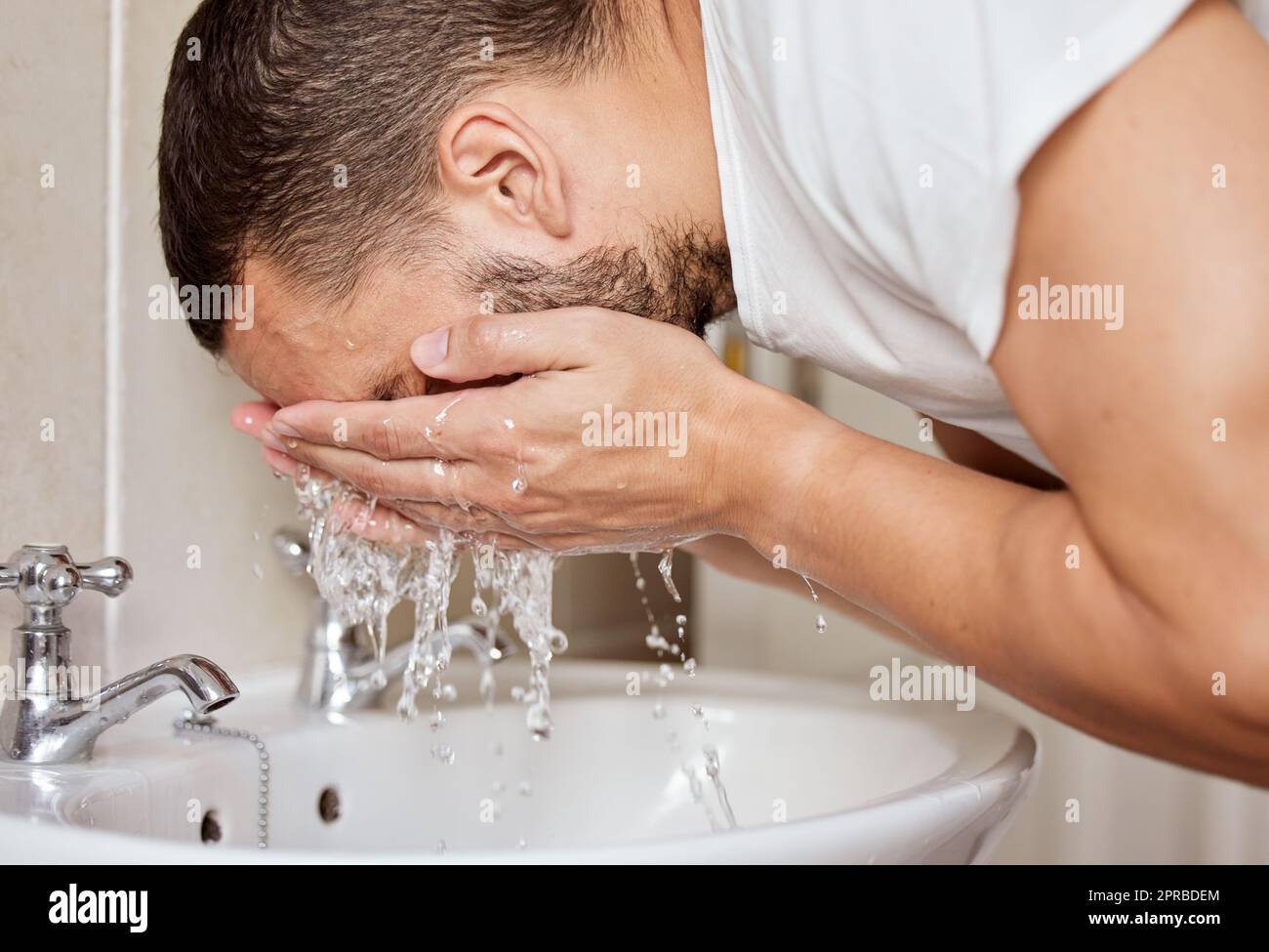Consistent skincare will leave you glowing. a young man washing his face in his bathroom sink ...