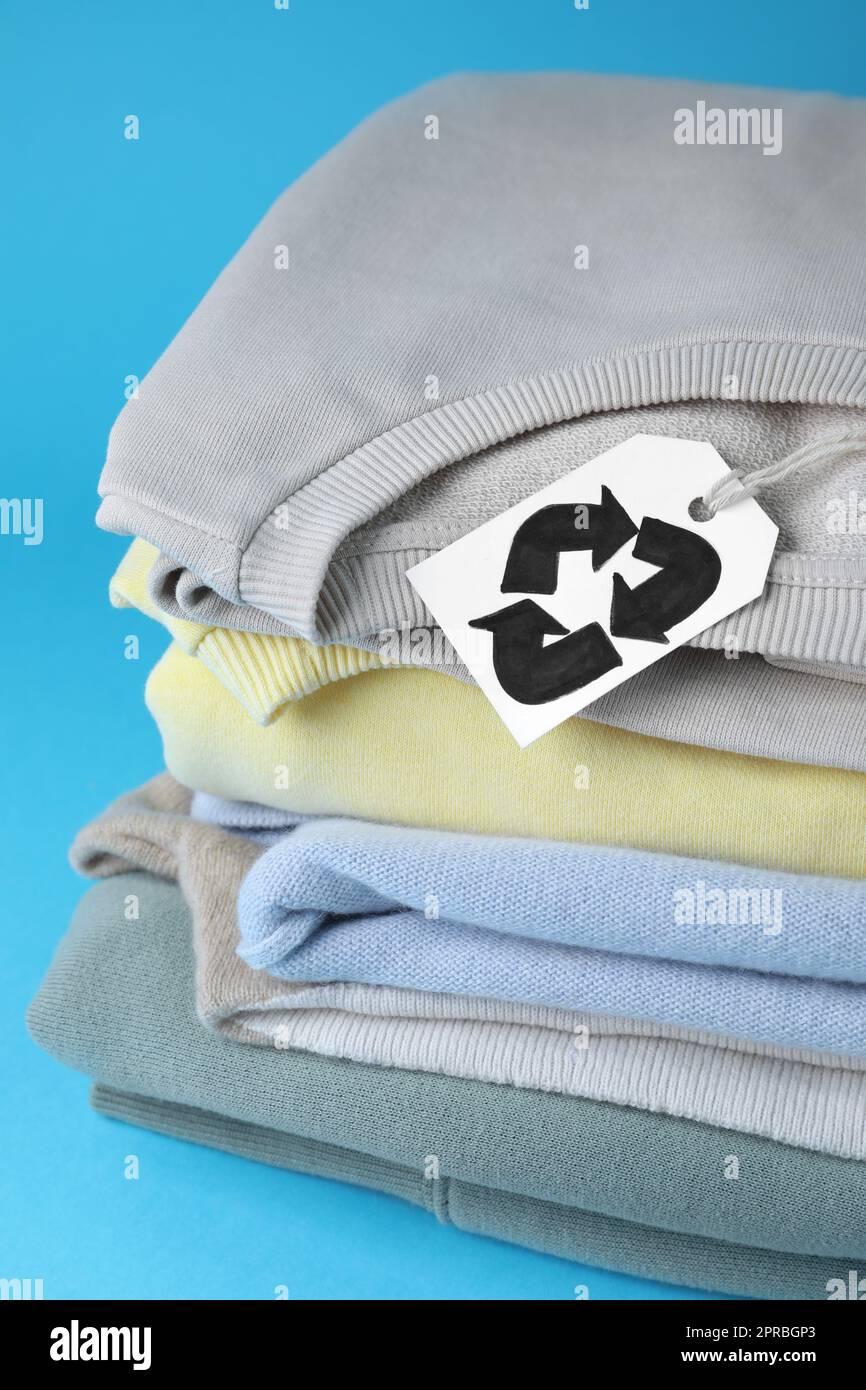 Stack of clothes with recycling label on light blue background, closeup ...