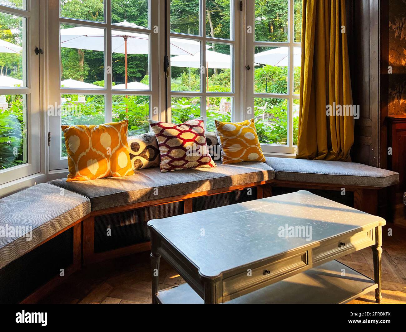 Wooden table near cozy bay window seat with cushions in room. Interior ... Wooden table near cozy bay window seat with cushions in room. Interior ...