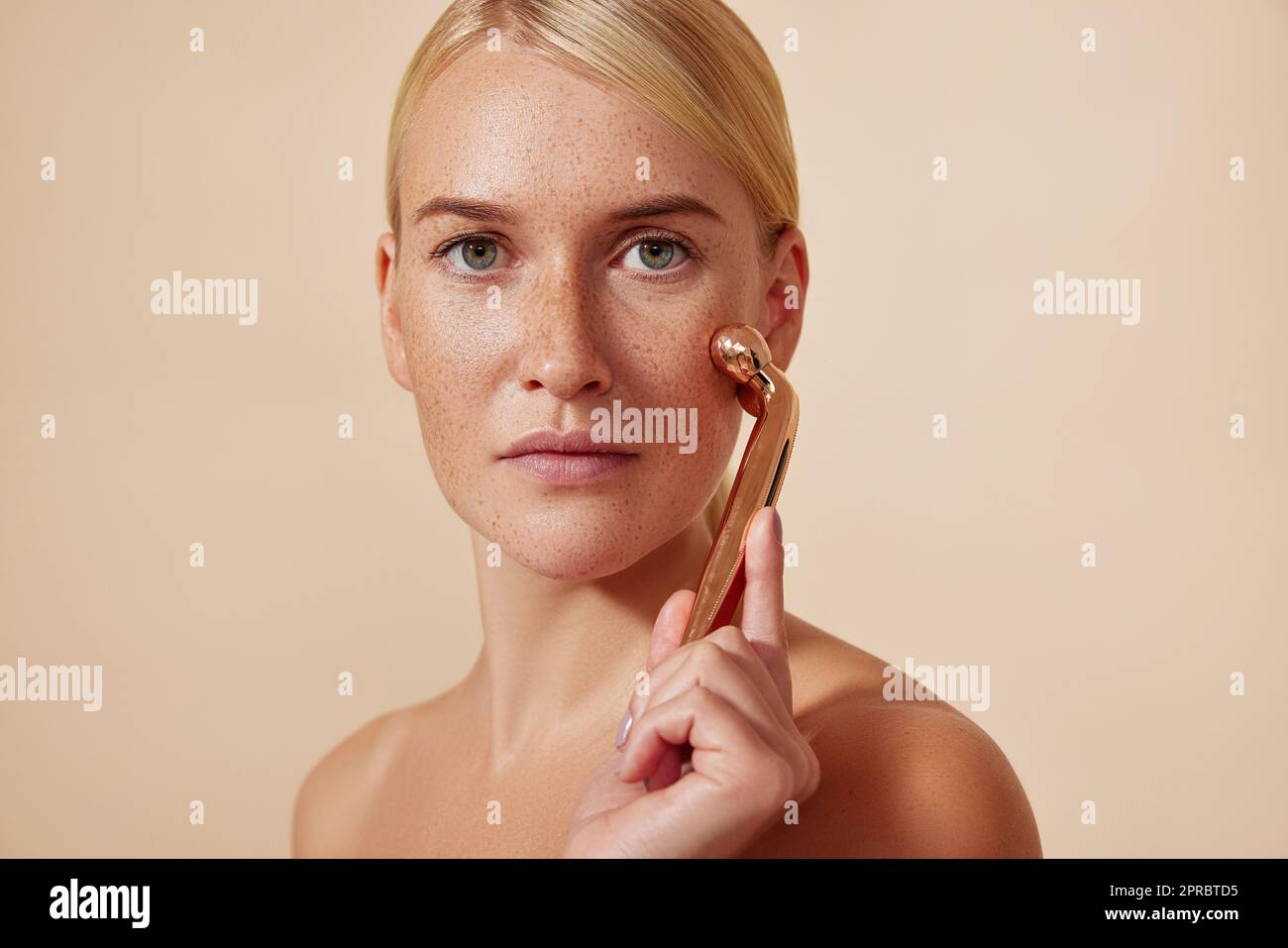 Young woman with smooth skin using a facial roller. Blond female doing ...