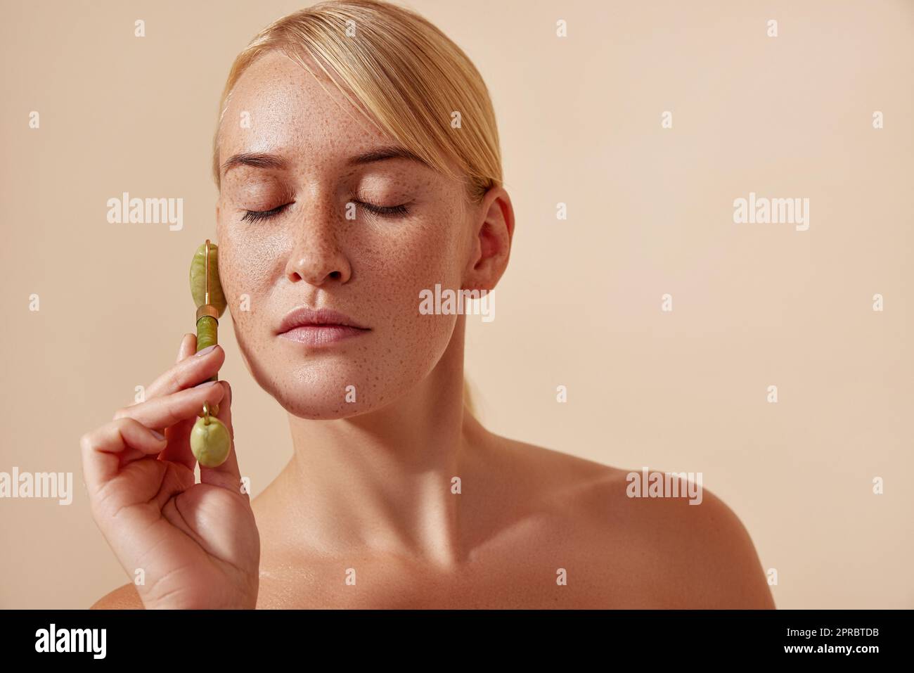 Beautiful woman with freckles using jade roller. Young female with ...