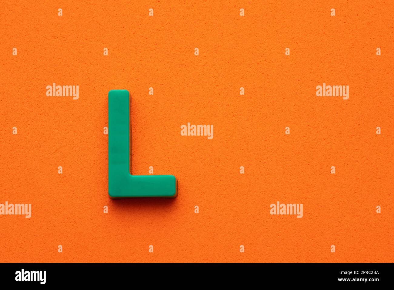 Alphabet letter L - Green plastic piece on orange foamy background ...