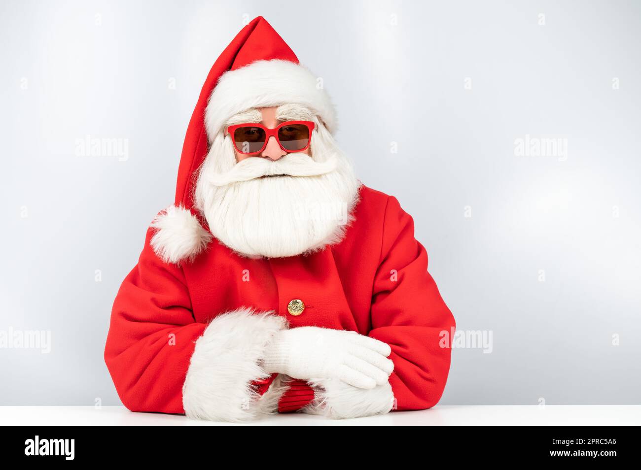 Portrait of santa claus sitting with his arms folded at a white table ...