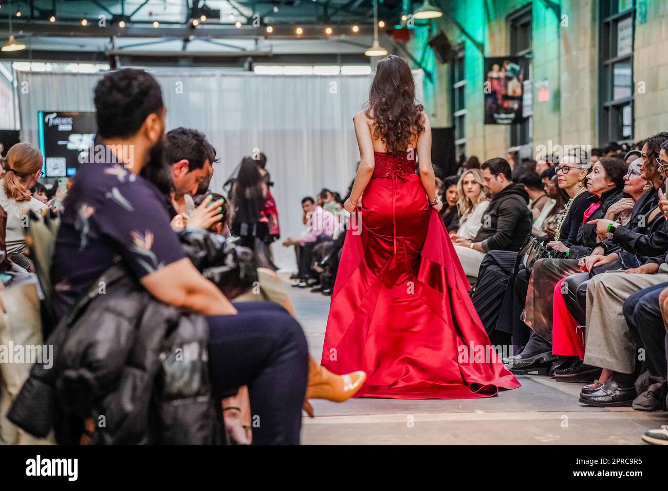 Behind a fashion model walking back on a runway with audience on both ...