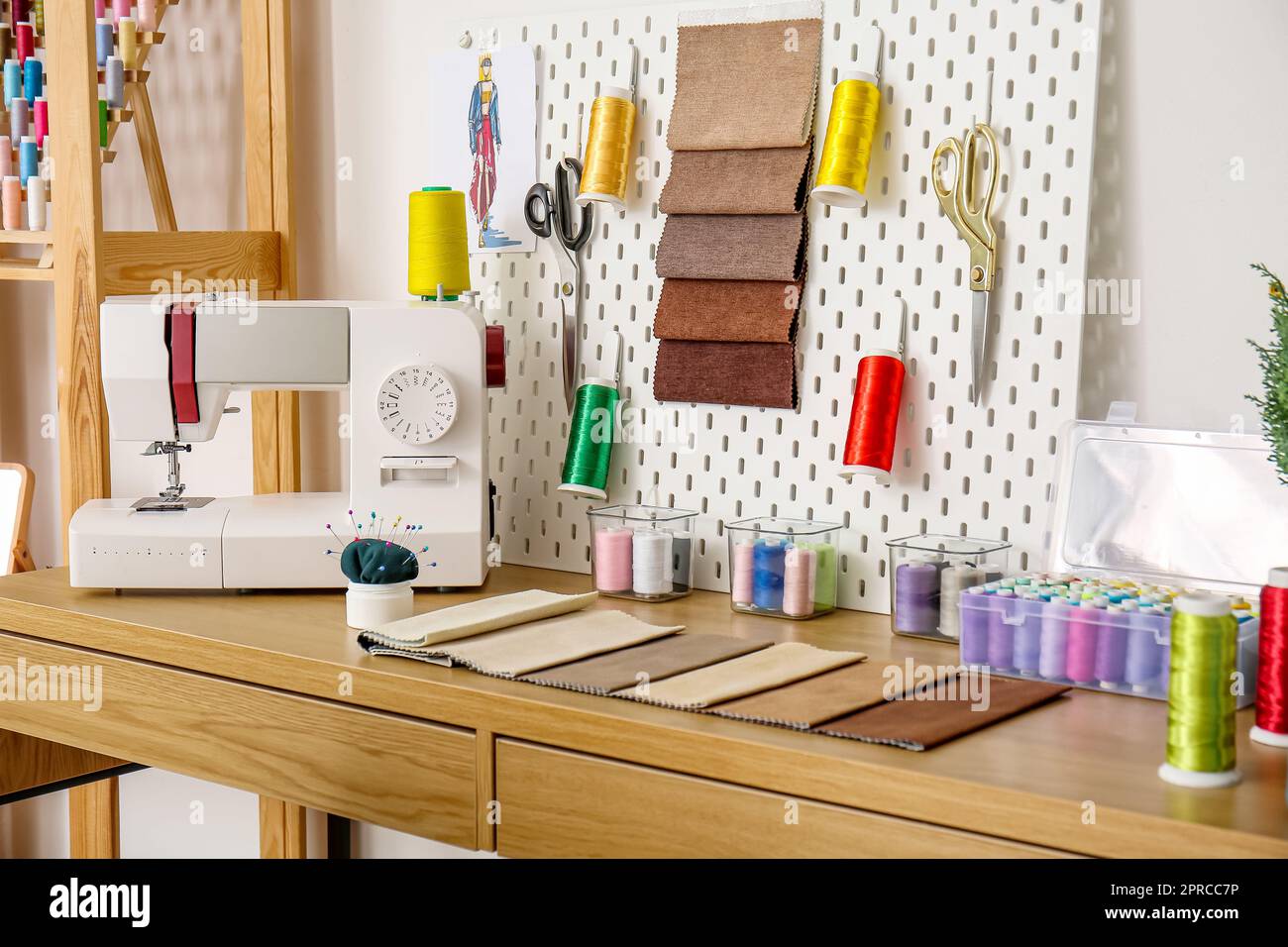 Tailor's workplace with sewing machine, thread spools and pegboard in ...